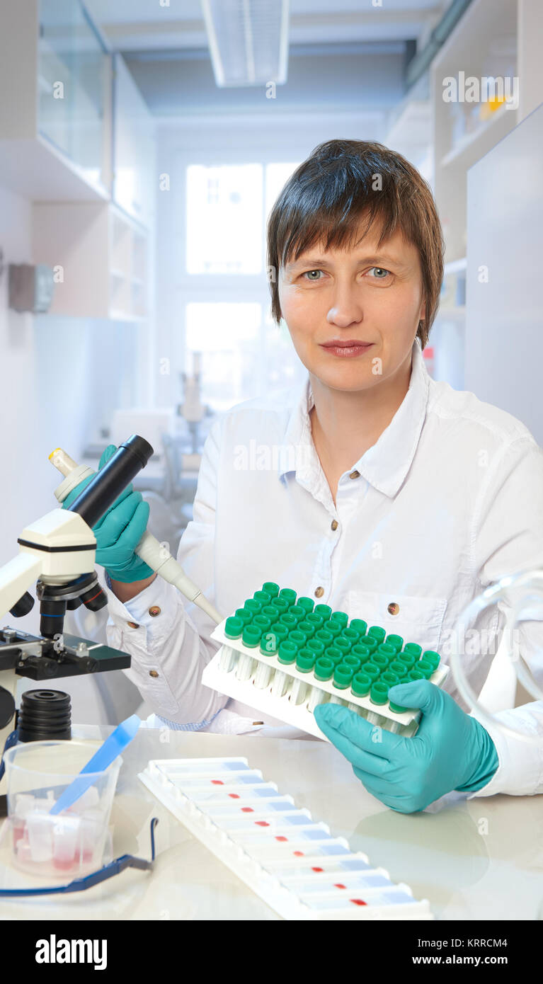 Middle-aged female scientist or tech with rack of plastic tubes and ...