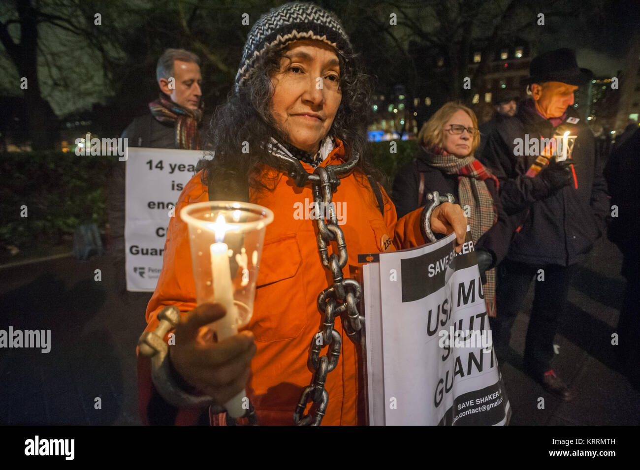 A woman in orange jump suit and chains holds a candle and a poster 'US ...