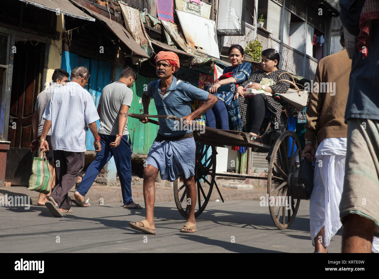 A hand-pulled rickshaw carrys passengers through the streets of Kolkata ...