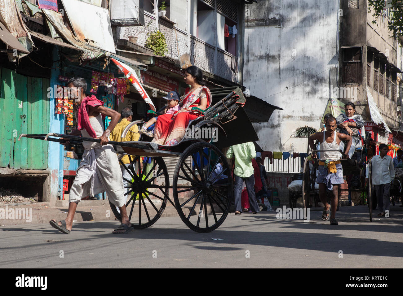 A hand-pulled rickshaw carrys passengers through the streets of Kolkata ...