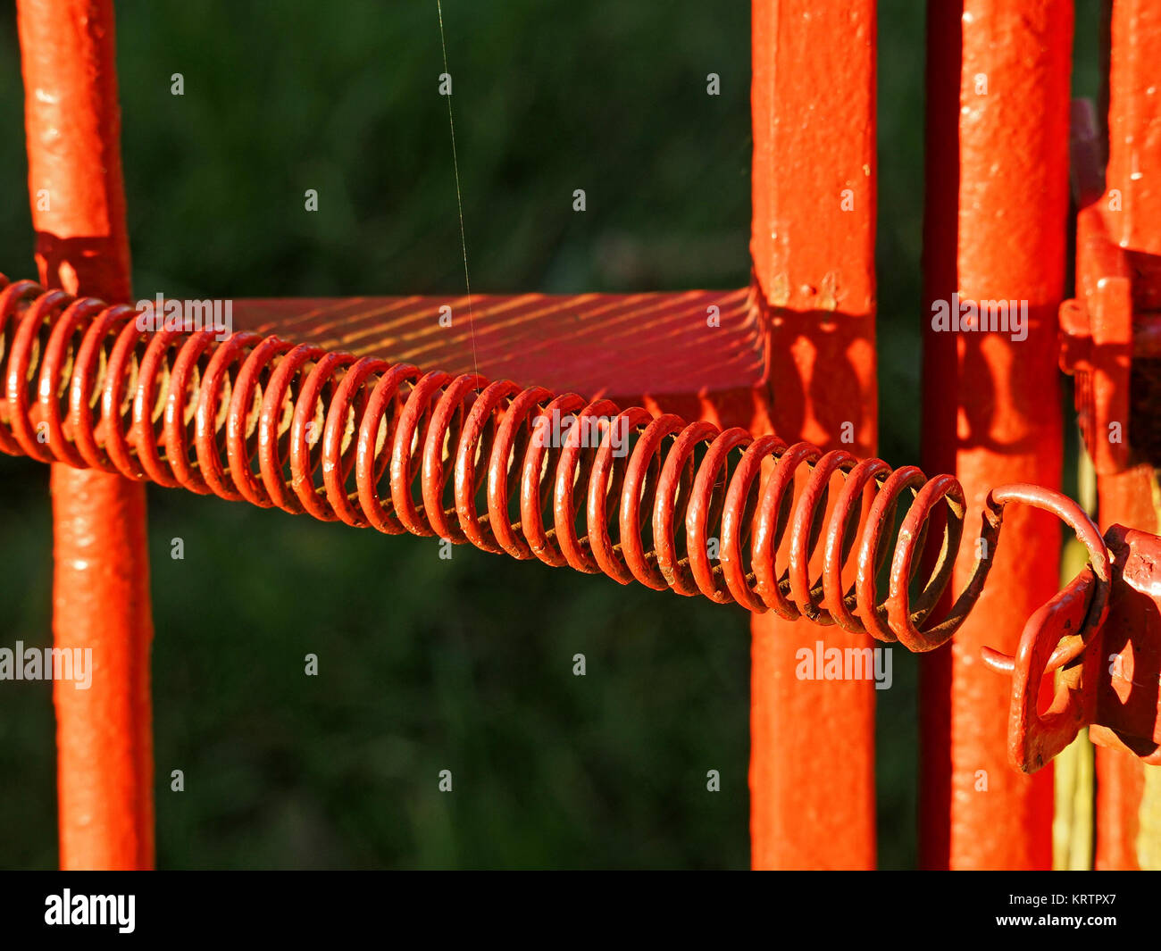 bright red spring connecting gate and gatepost casts shadow on ...