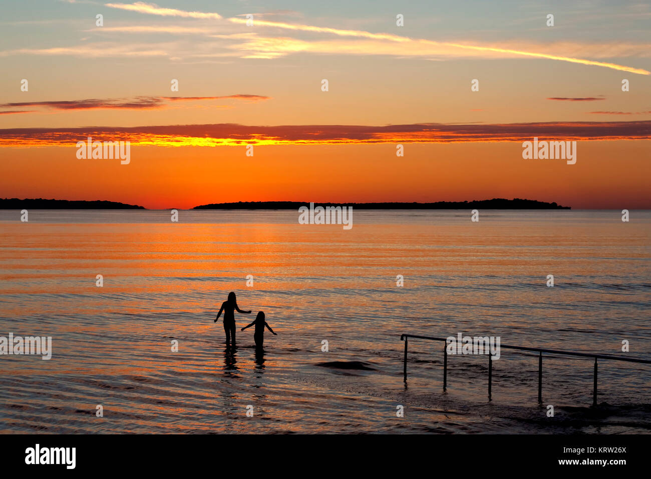 Two girls going out of the sea with sunset in background Stock Photo ...