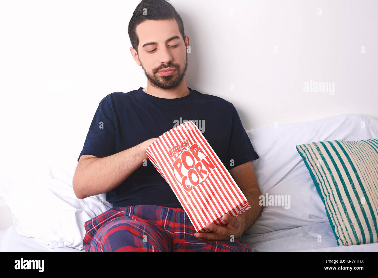 Young man eating popcorn and watching movies relaxed on bed. Indoors ...
