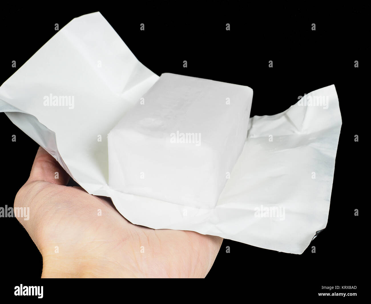 Unwrapped block of coconut fat in aluminium paper held by a person ...