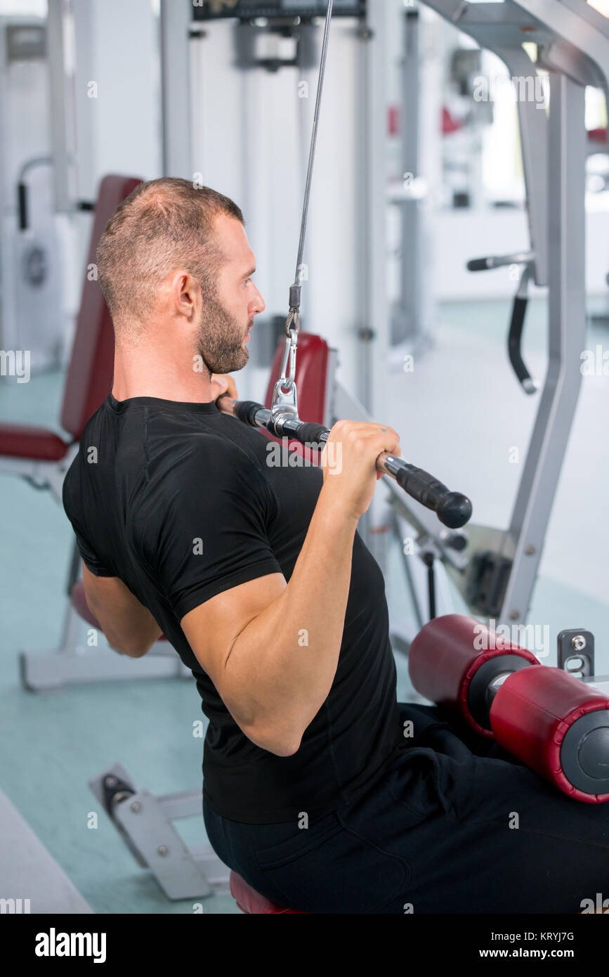 Determined young muscular man working on fitness machine at the gym ...