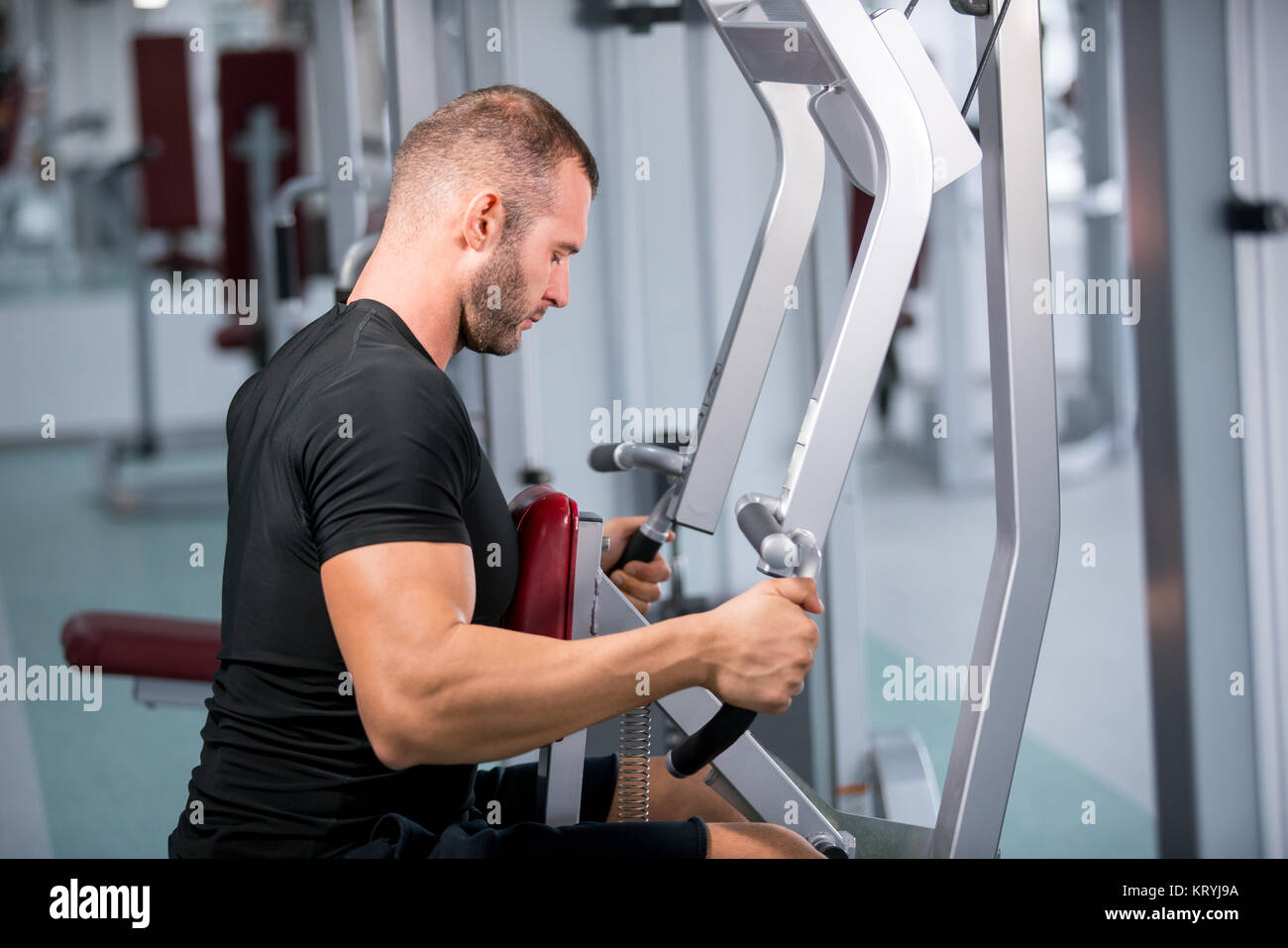 Determined young muscular man working on fitness machine at the gym ...
