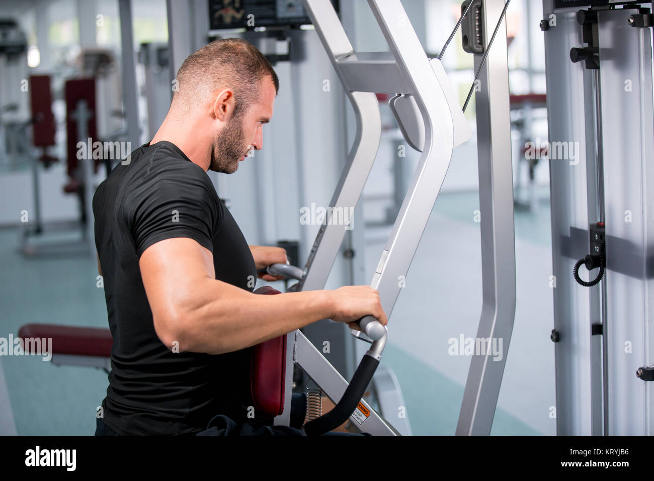 Determined young muscular man working on fitness machine at the gym ...
