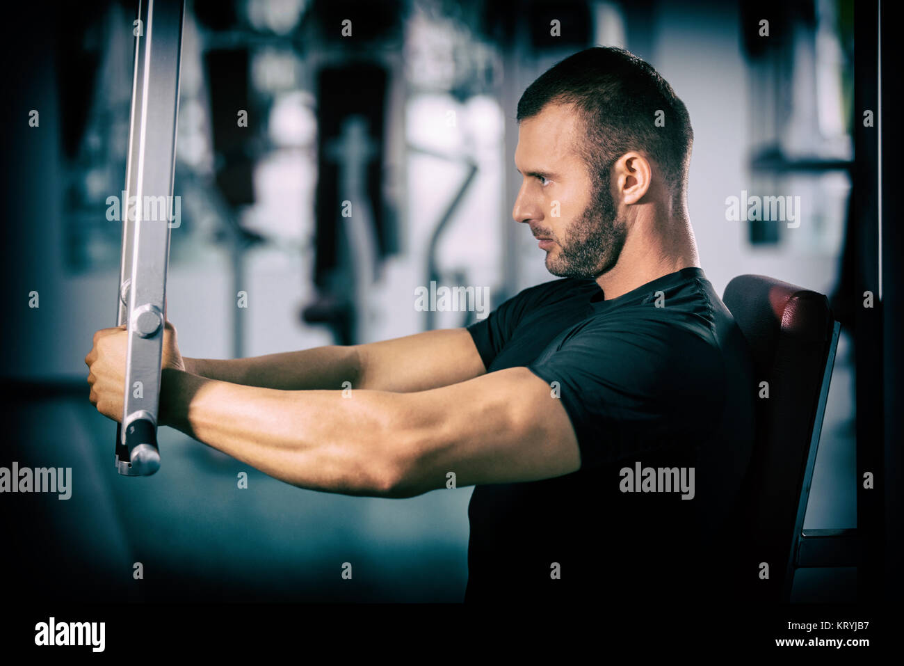 Determined young muscular man working on fitness machine at the gym ...