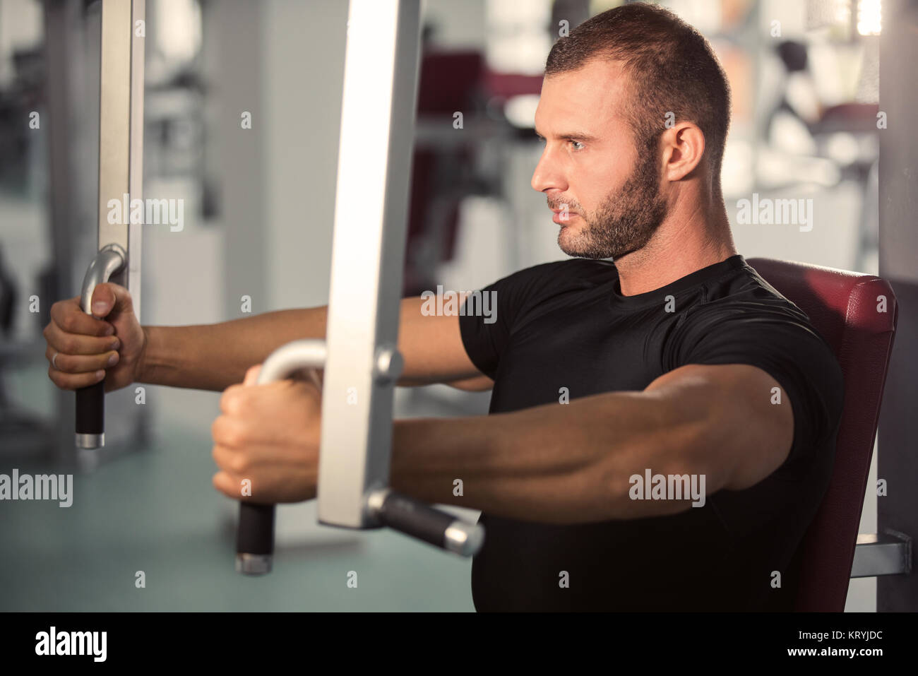 Determined young muscular man working on fitness machine at the gym ...