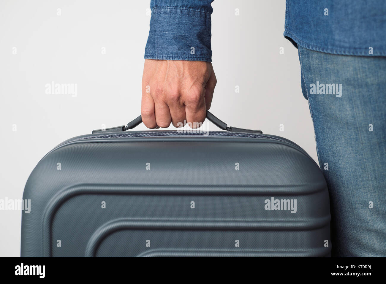 closeup of a young caucasian man carrying a suitcase by its handle ...