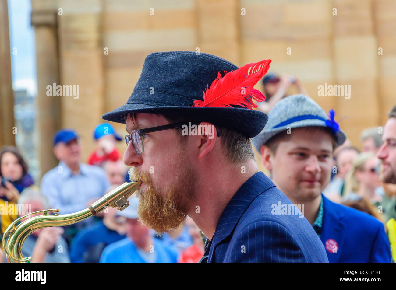 Male musician wearing a trilby hat with red feather playing a saxophone ...