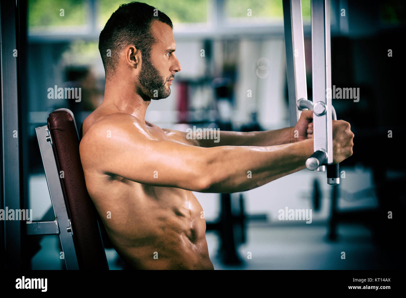 Determined young muscular man working on fitness machine at the gym ...