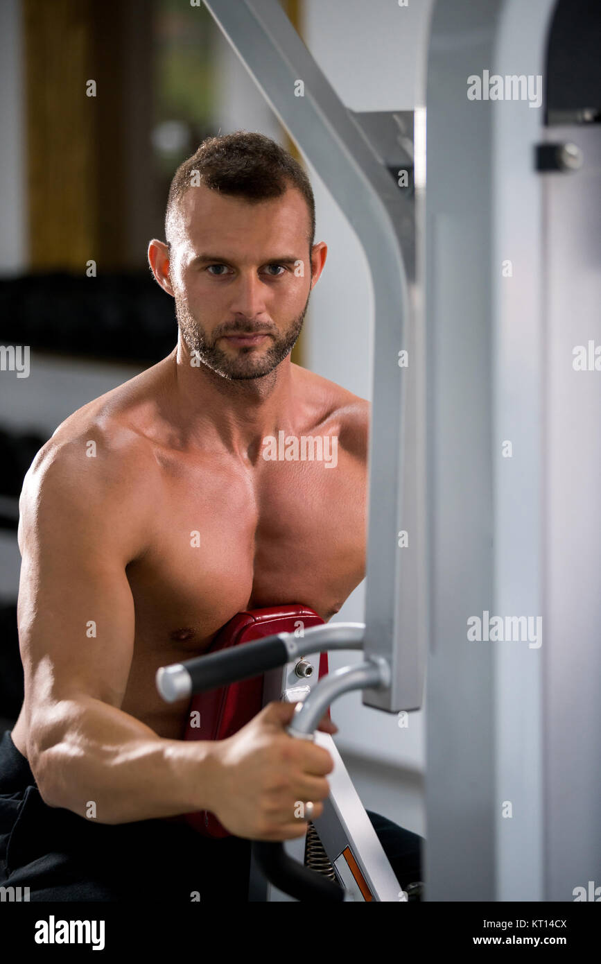 Determined young muscular man working on fitness machine at the gym ...