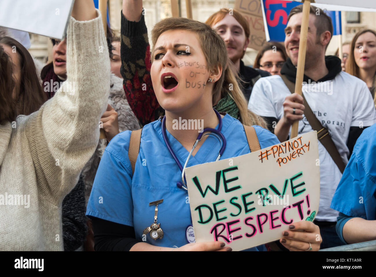 A nurse in uniform with hashtag on her cheek and poster 'We Seserve ...