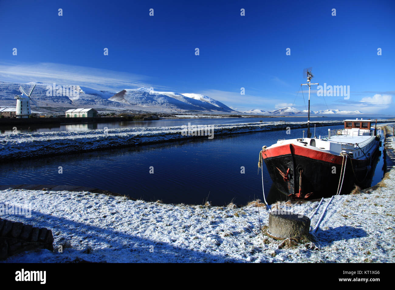 large river barge tied to pier wall with the snow covered mountains in ...