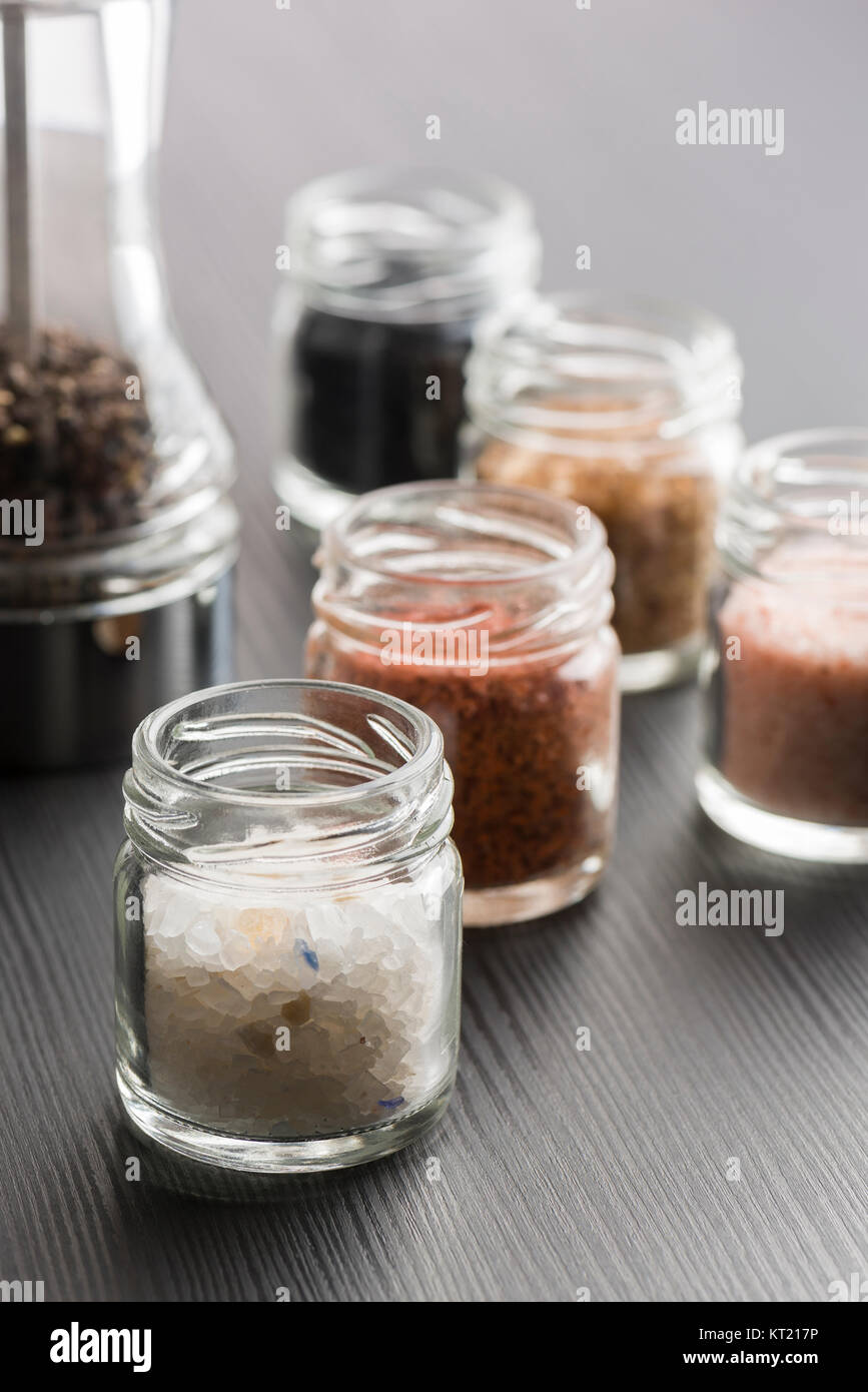 variety of natural and spicy salt into glass jars on black table Stock ...