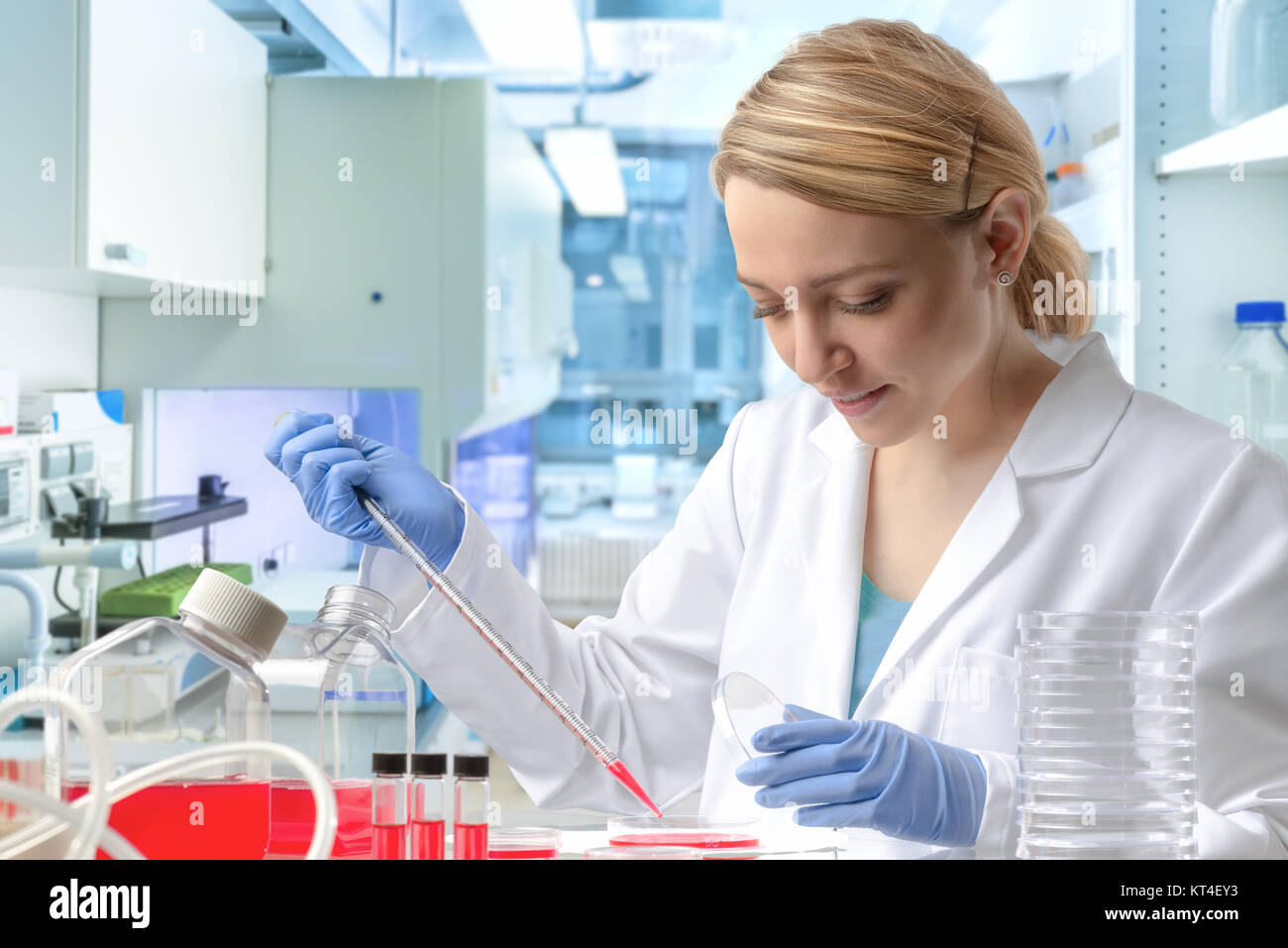 Young European female scientist or tech in white coat and blue gloves ...