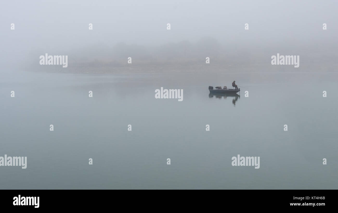 Fisherman on Boat in the Middle of Large Lake with Dense Fog Around him ...