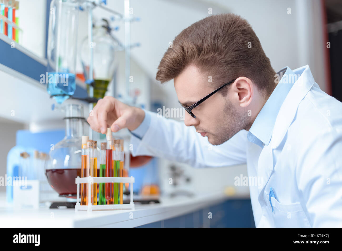 Side view of young man scientist holding test tube with reagent in lab ...