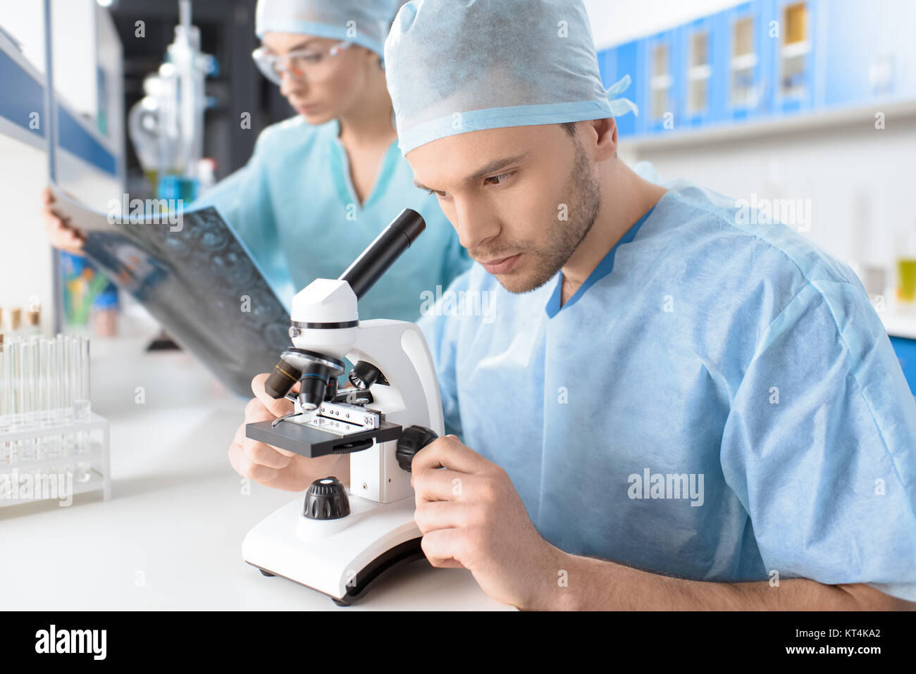 side view of surgeon looking through microscope and doctor analyzing x ...