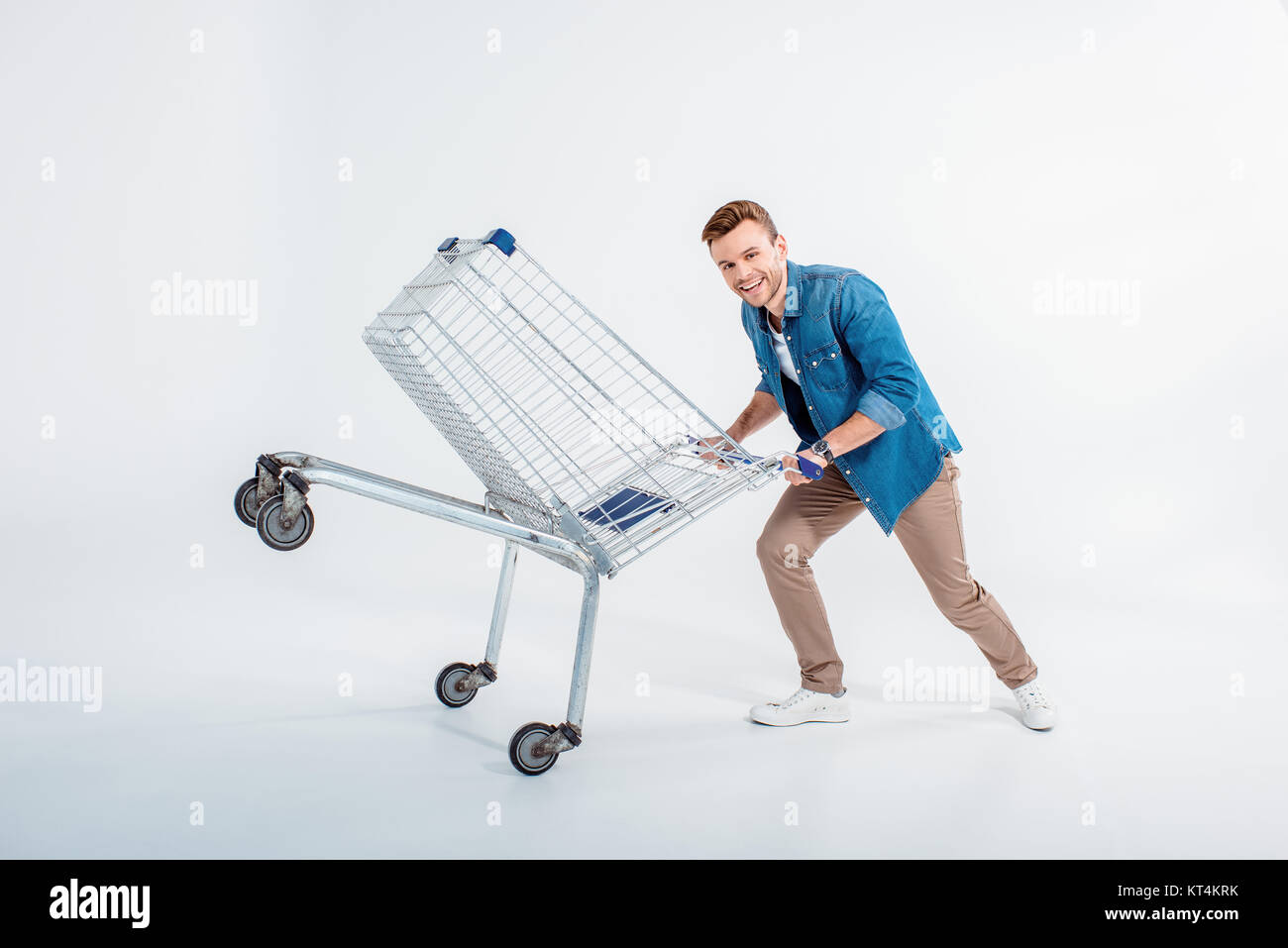 Excited young man having fun with shopping trolley on white Stock Photo ...
