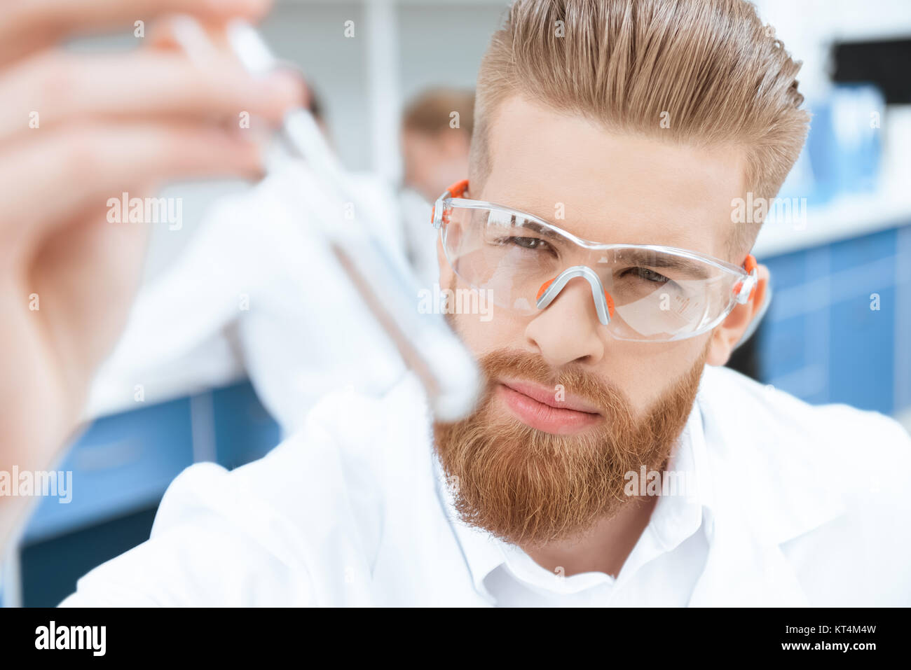 Close-up view of bearded chemist in protective goggles inspecting test ...