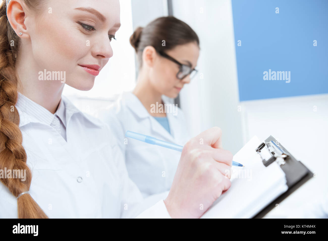 Young women scientists in white coats taking notes in laboratory Stock ...