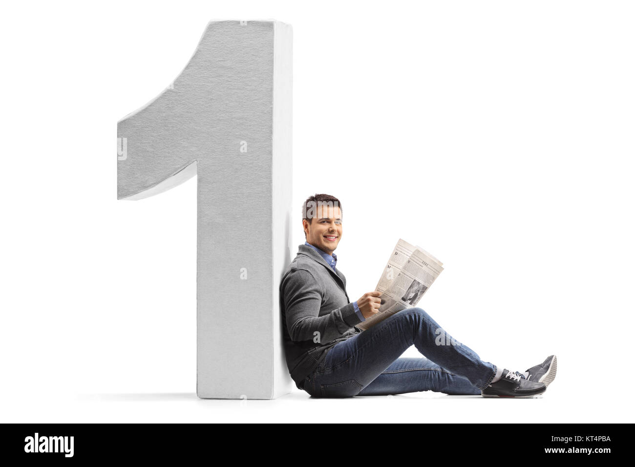 Young man with a newspaper leaning against a cardboard number one ...