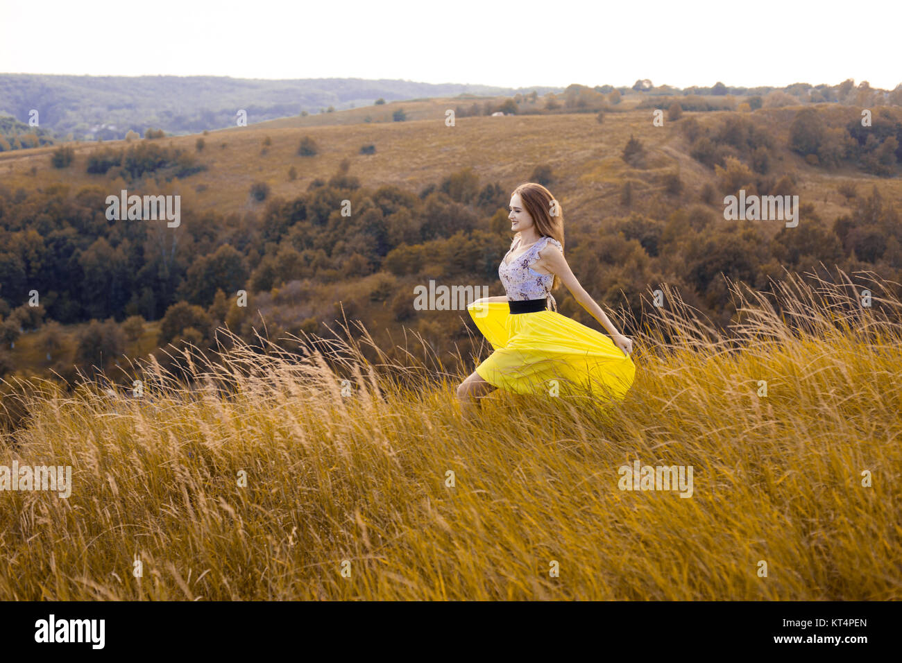 Happy playful young pretty girl running on the field with green, yellow ...
