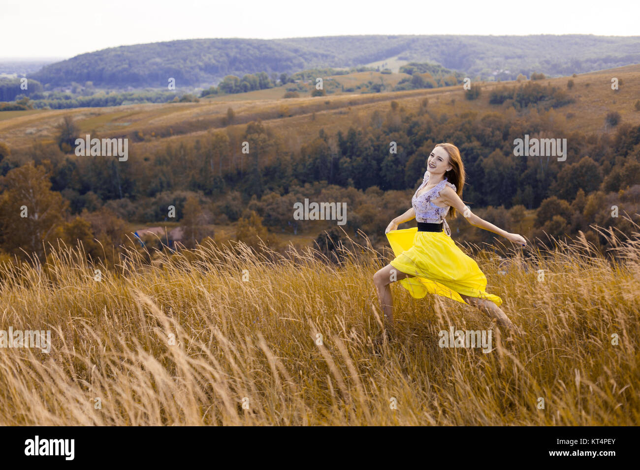 Happy playful young pretty girl running on the field with green, yellow ...