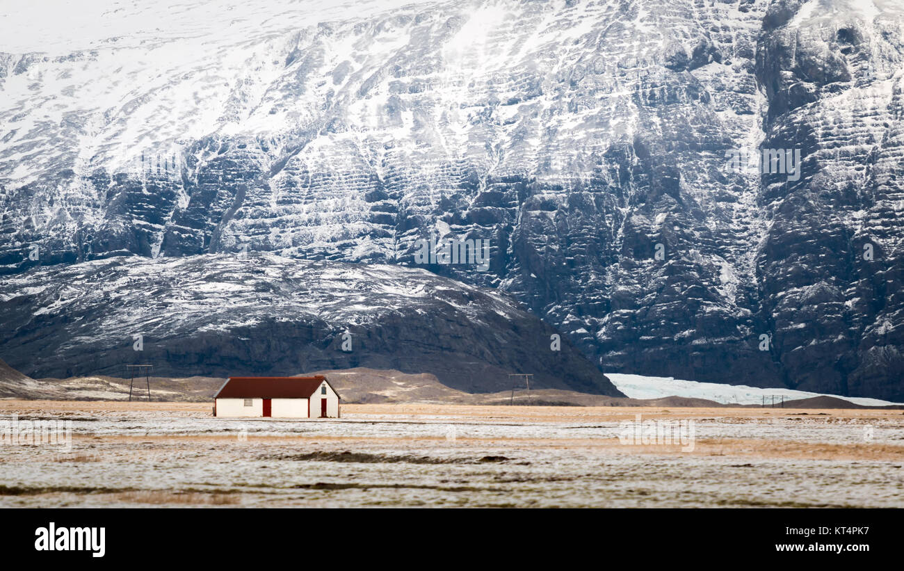 Iceland landscape-- small farmhouse on the plain dwarfed by enormous ...