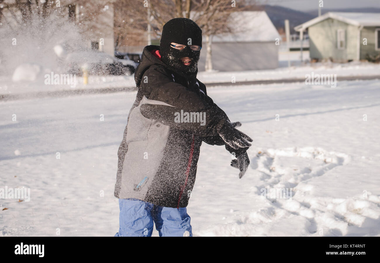 A young boy wearing a winter ski mask plays in the snow during the day ...