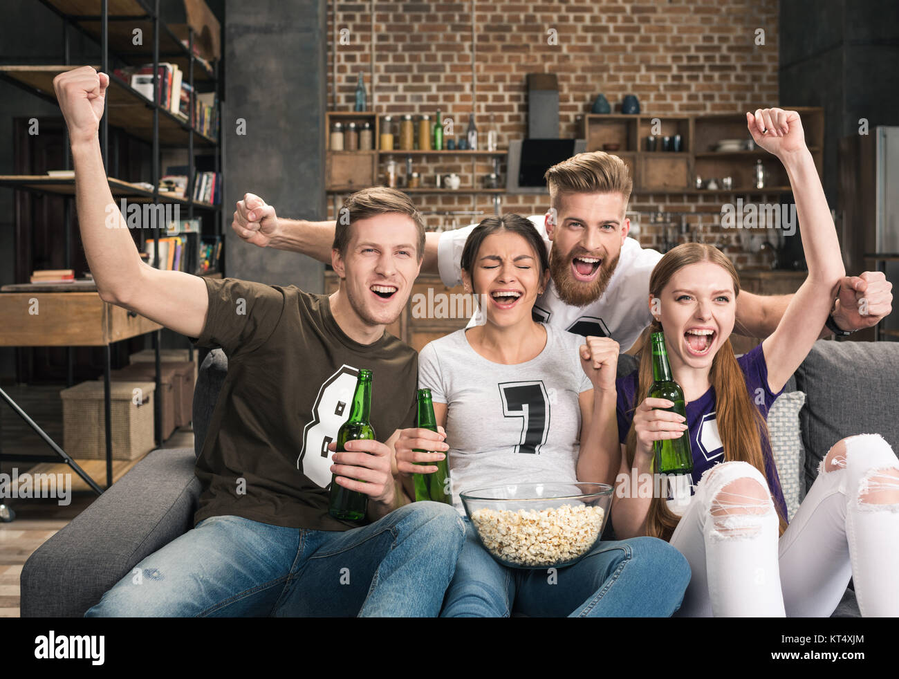 Excited young friends drinking beer and eating popcorn while supporting ...