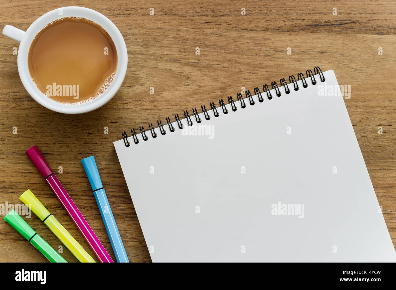 Wooden desk table with notebook, color pens and cup of coffee. Top view ...