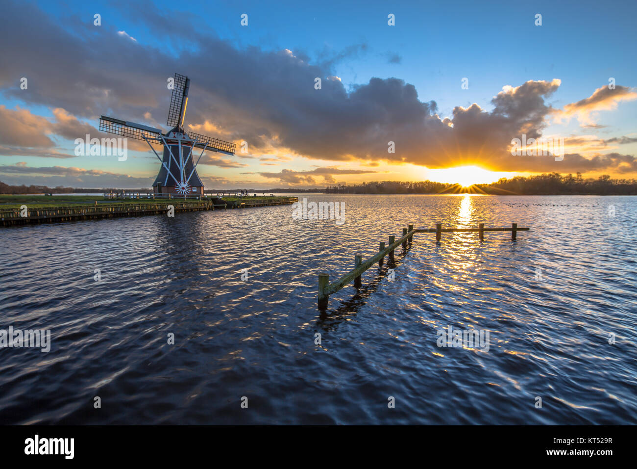 Tradional wooden windmill on the waterfront of a lake under cloudy ...