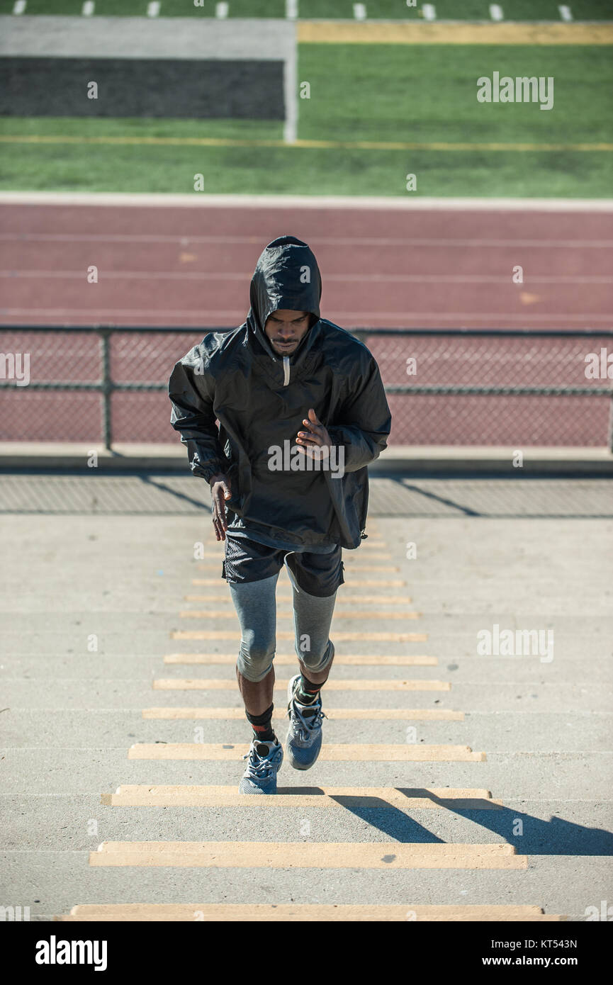 Hooded lean athlete warming up for workout on concrete steps of stadium ...