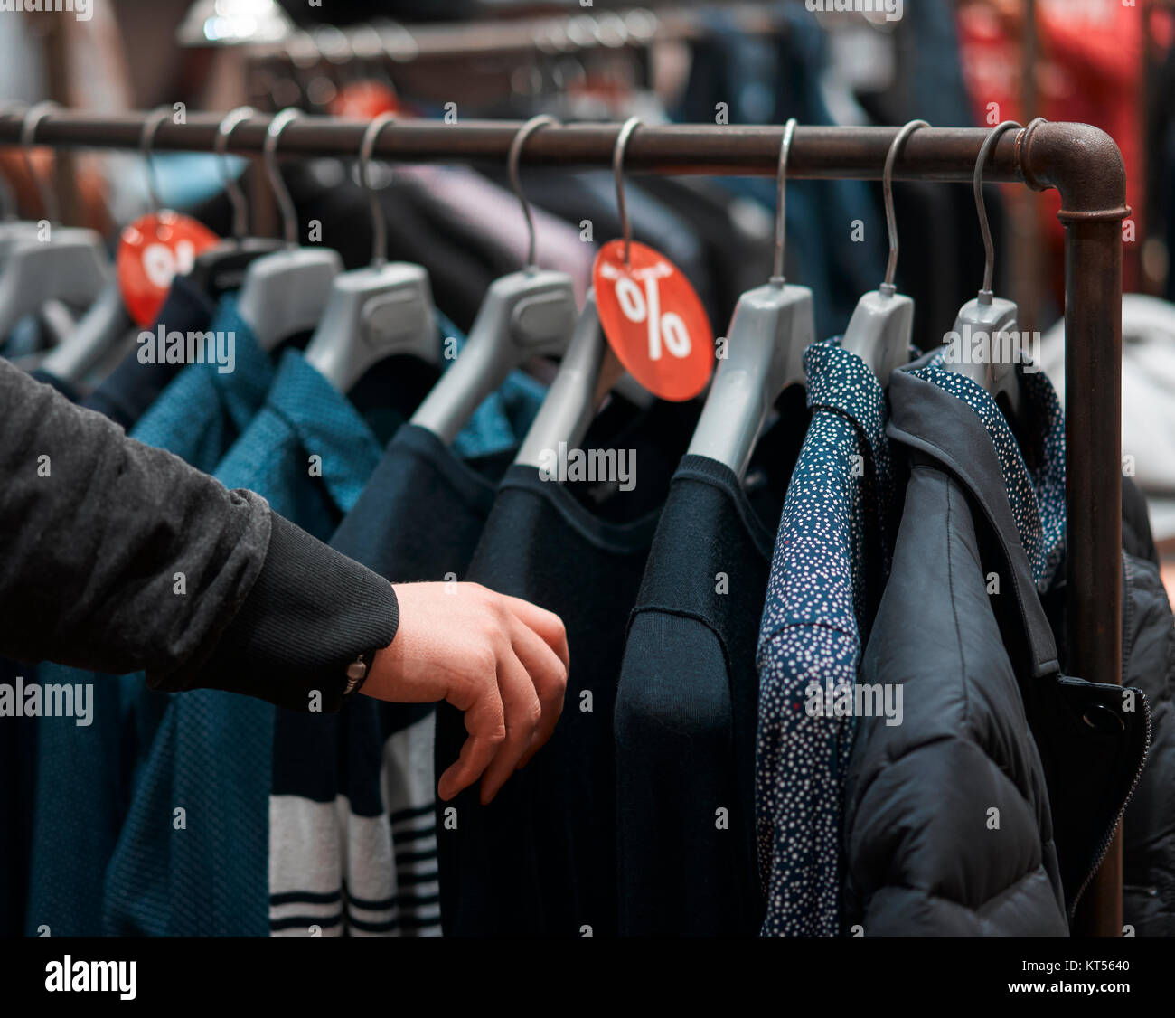 man chooses the clothes hanging on hangers in shop Stock Photo - Alamy
