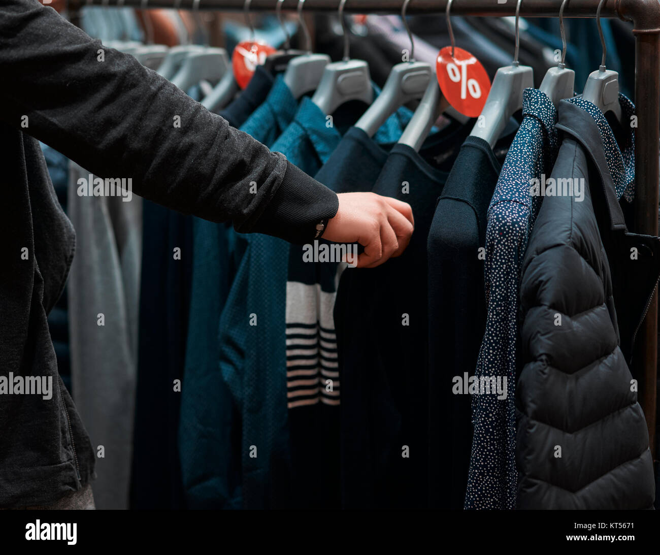 man chooses the clothes hanging on hangers in shop Stock Photo - Alamy