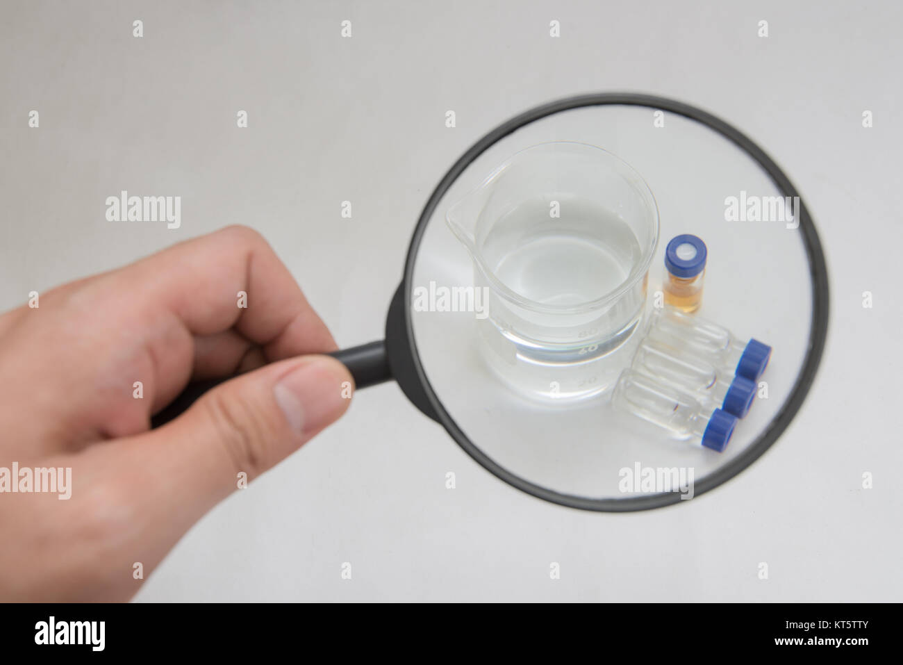 Handing magnify glass on sample vial and beaker Stock Photo - Alamy