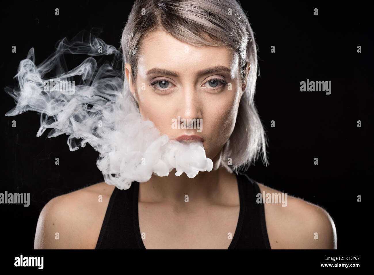 Attractive young woman vaping and blowing smoke on black Stock Photo ...