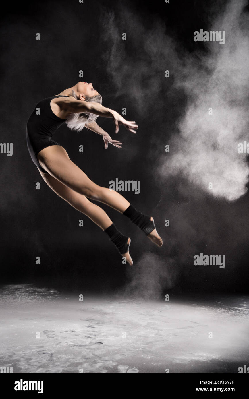 side view of woman in bodysuit with dust dancing on black Stock Photo ...