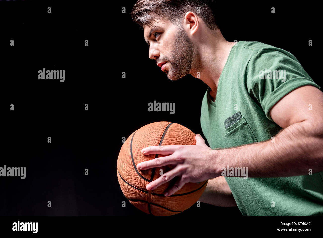 side view of concentrated man holding basketball ball on black Stock ...