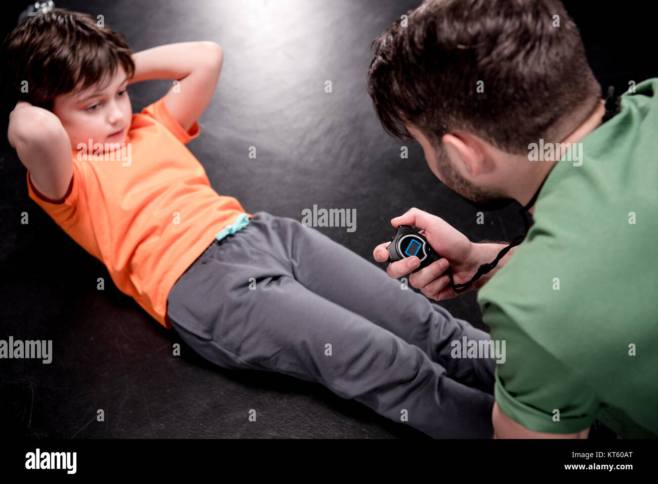 man controlling time while boy doing press exercise on black Stock ...