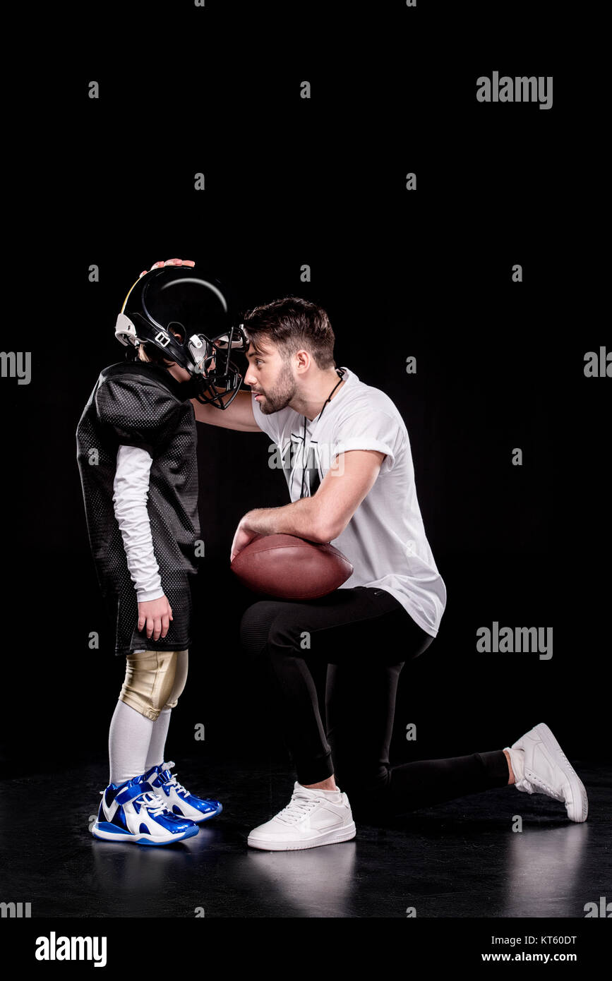 Side view of trainer instructing boy american football player on black ...