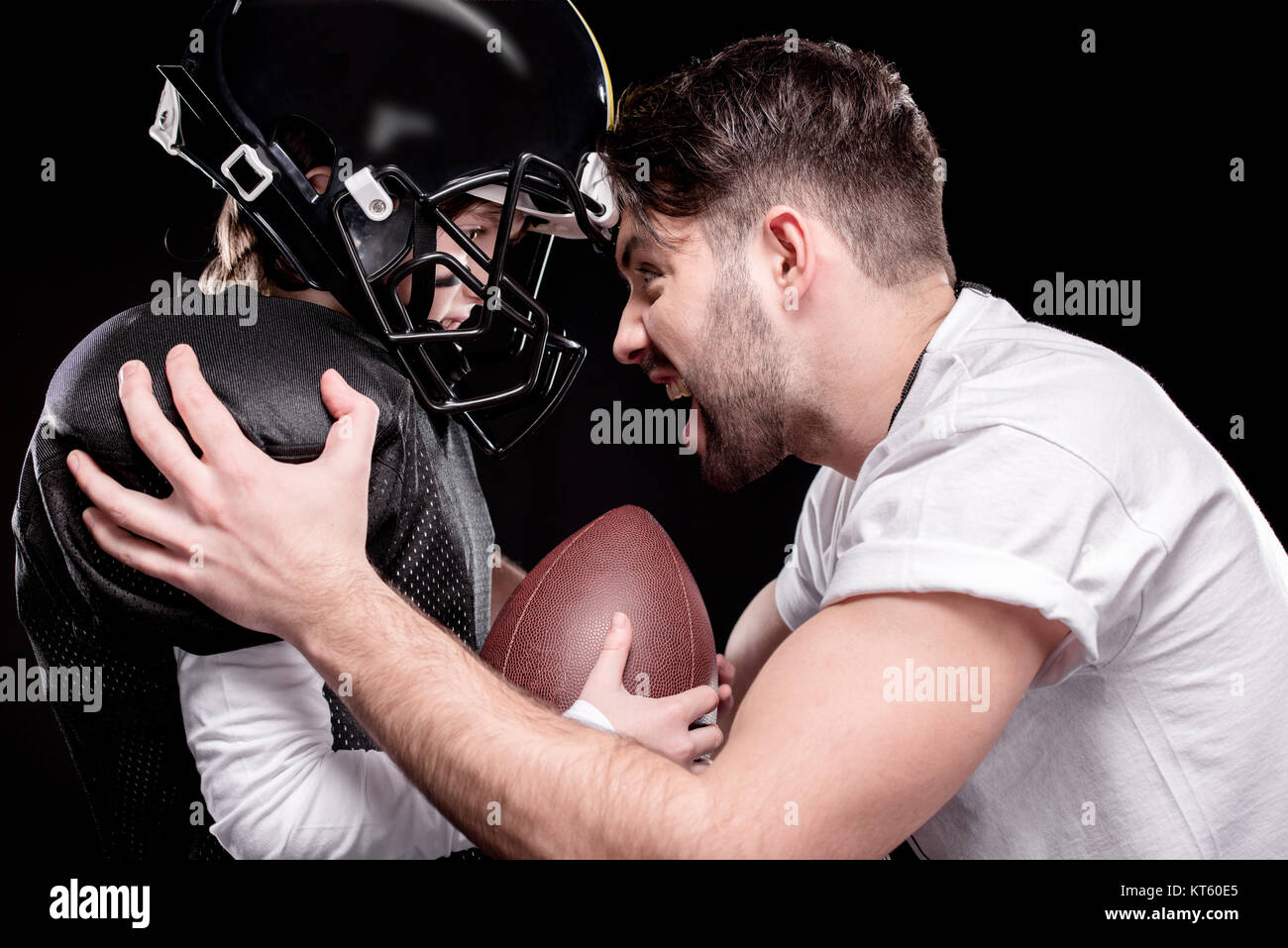 Side view of trainer screaming at boy american football player on black ...