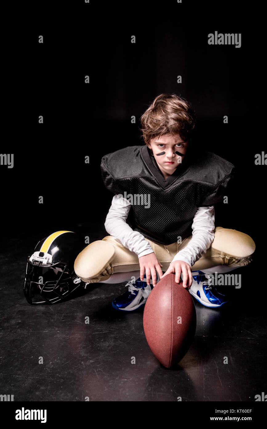 Serious little boy american football player crouching with ball and ...