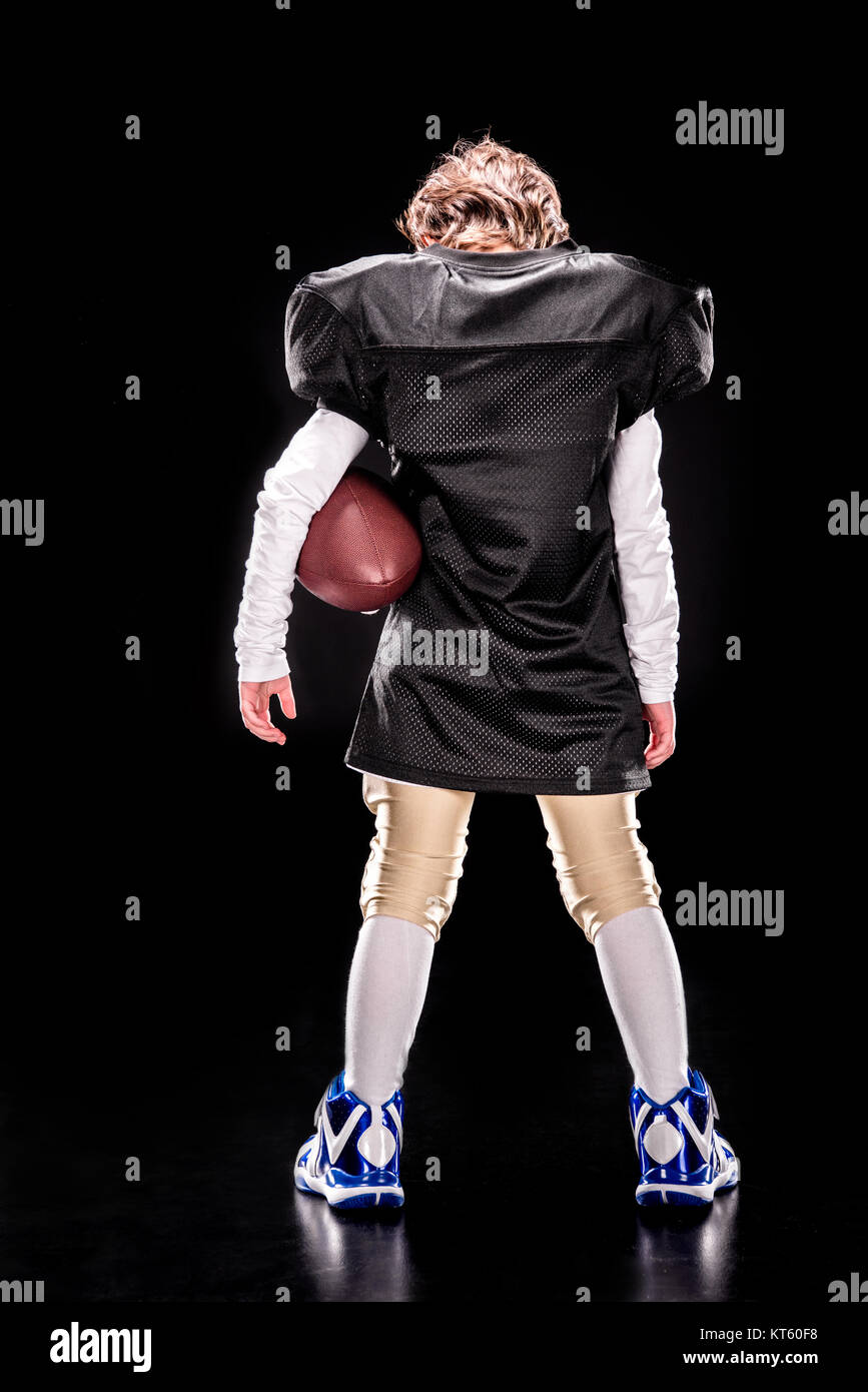 Back view of little boy american football player standing with ball on ...