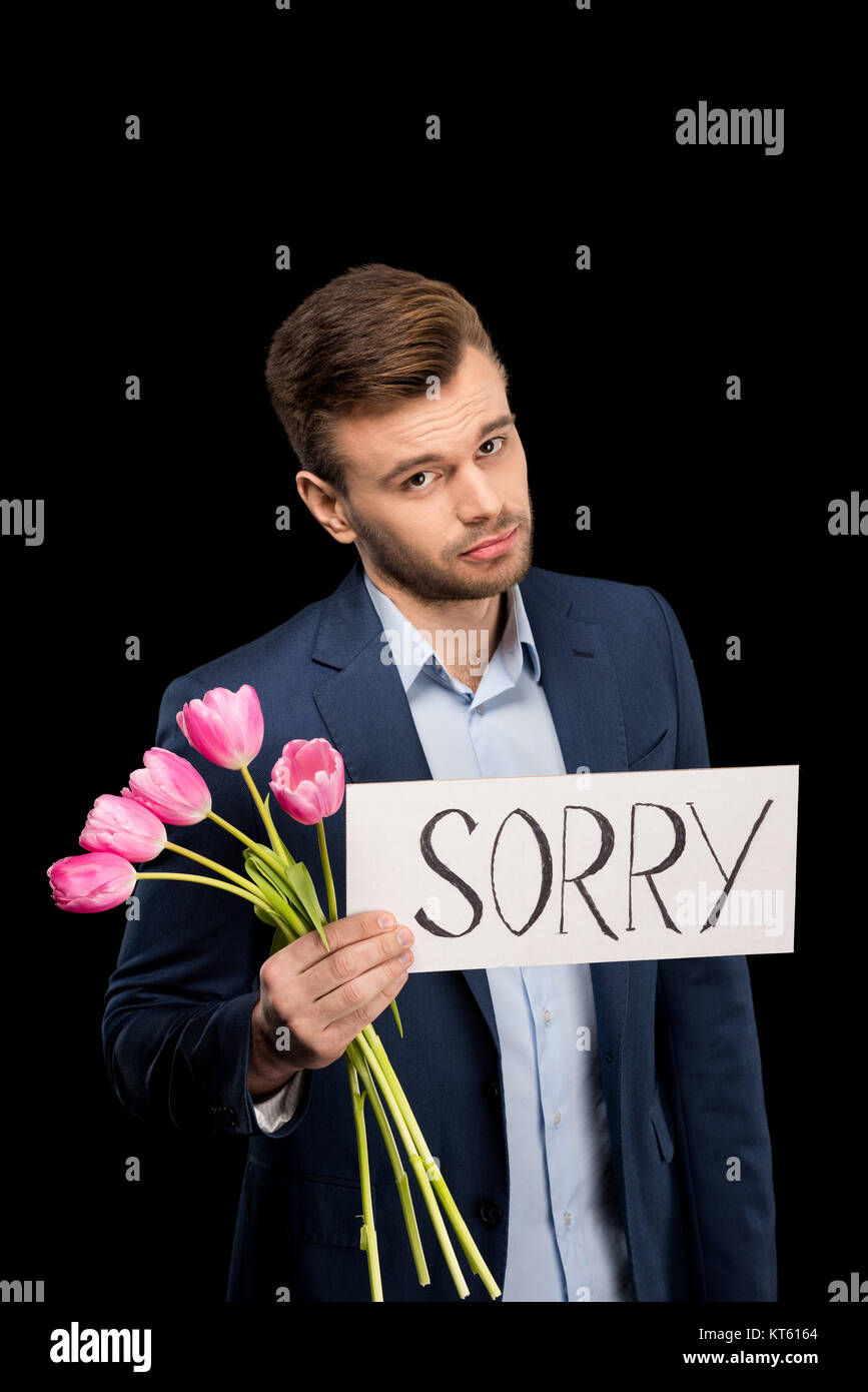 Upset young man holding pink tulips and sorry sign on black Stock Photo ...