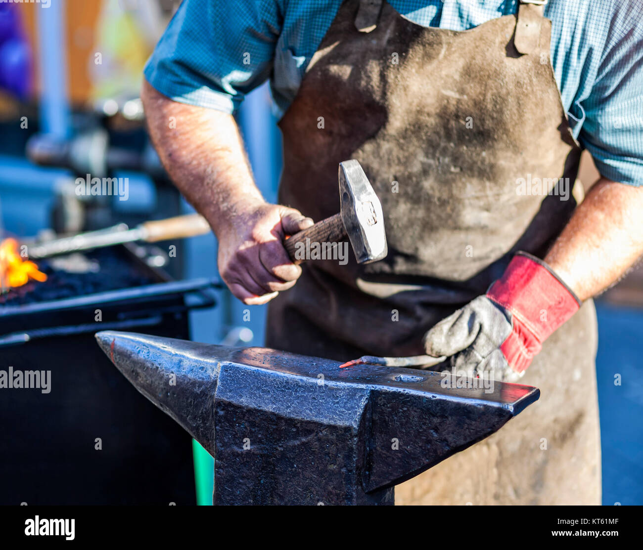 Blacksmith hammering red hot iron rod on anvil against the background ...