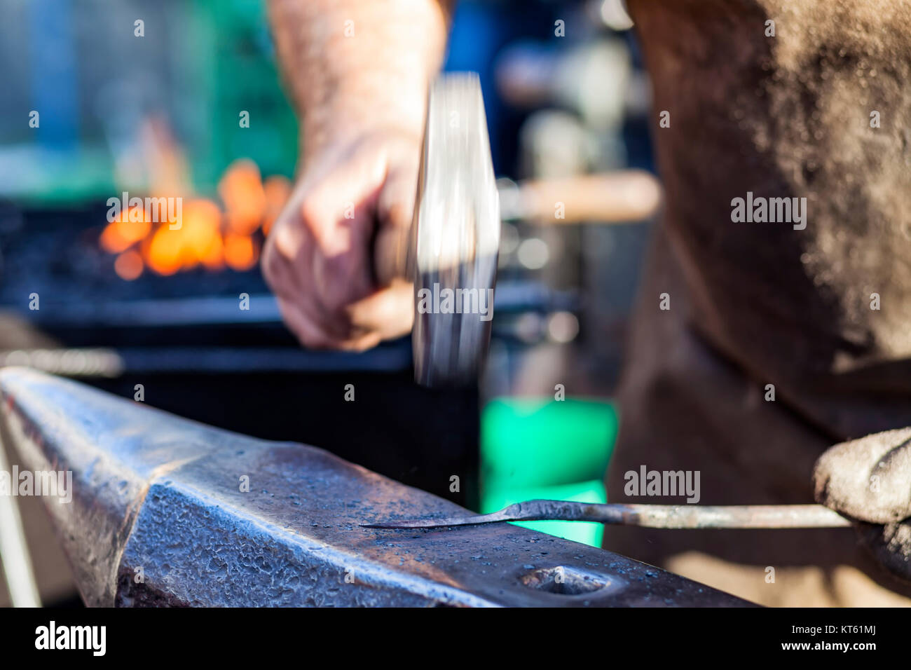 Blacksmith hammering hot iron rod on anvil against the background of ...